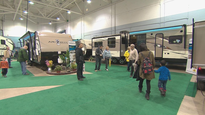 Une salle d'exposition avec des véhicules récréatifs, et des passants.