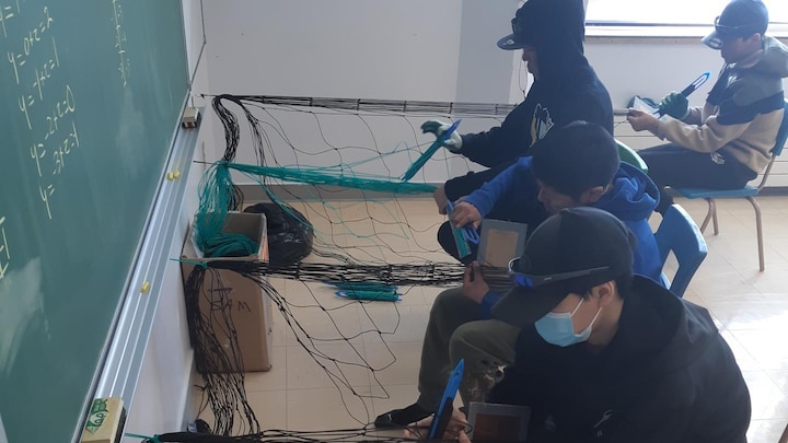 Des élèves fabriquent des filets de pêche dans une salle de classe.